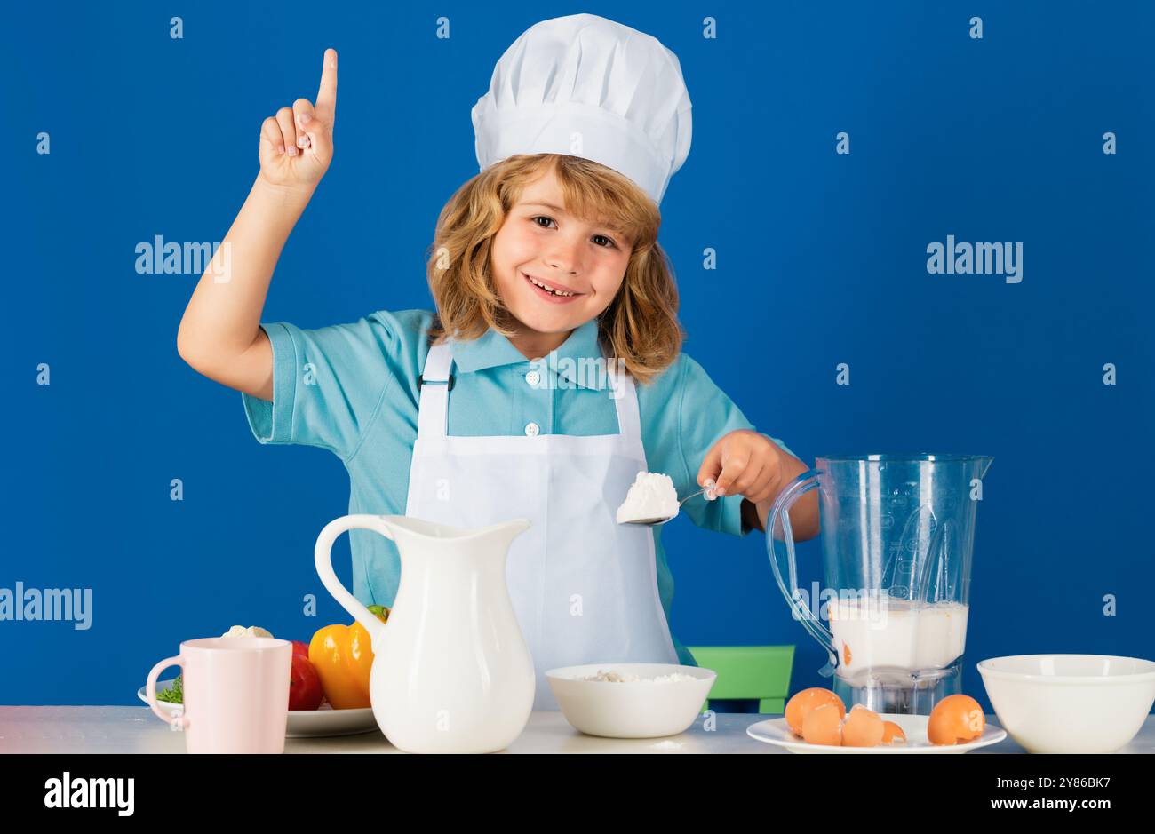 Child chef cook prepares food with flour in isolated blue studio ...