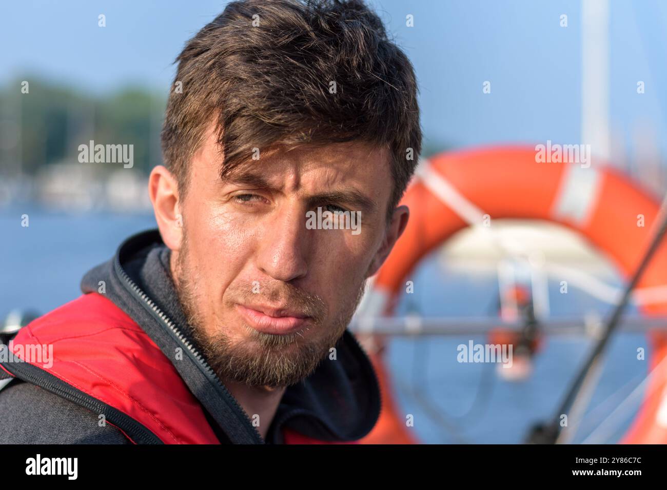 A thoughtful handsome young brunette man in front of a lifebuoy on a ...