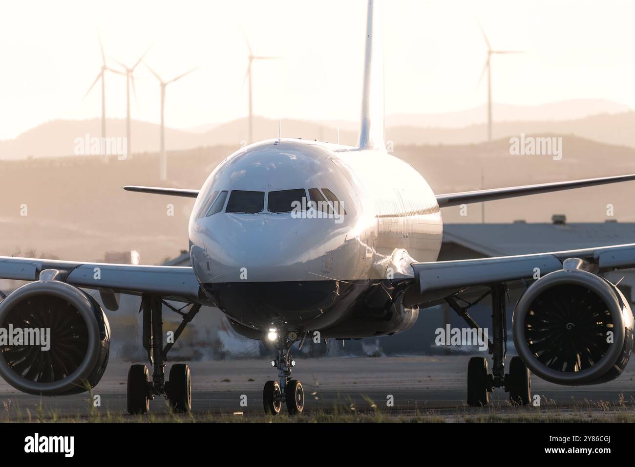 Passenger airplane at airport runway with wind turbines in background ...