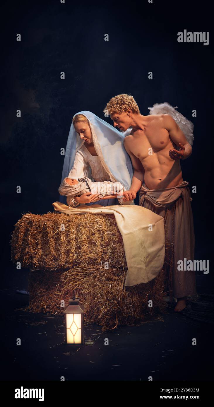 Mary holding baby Jesus in a manger with angel standing by ...