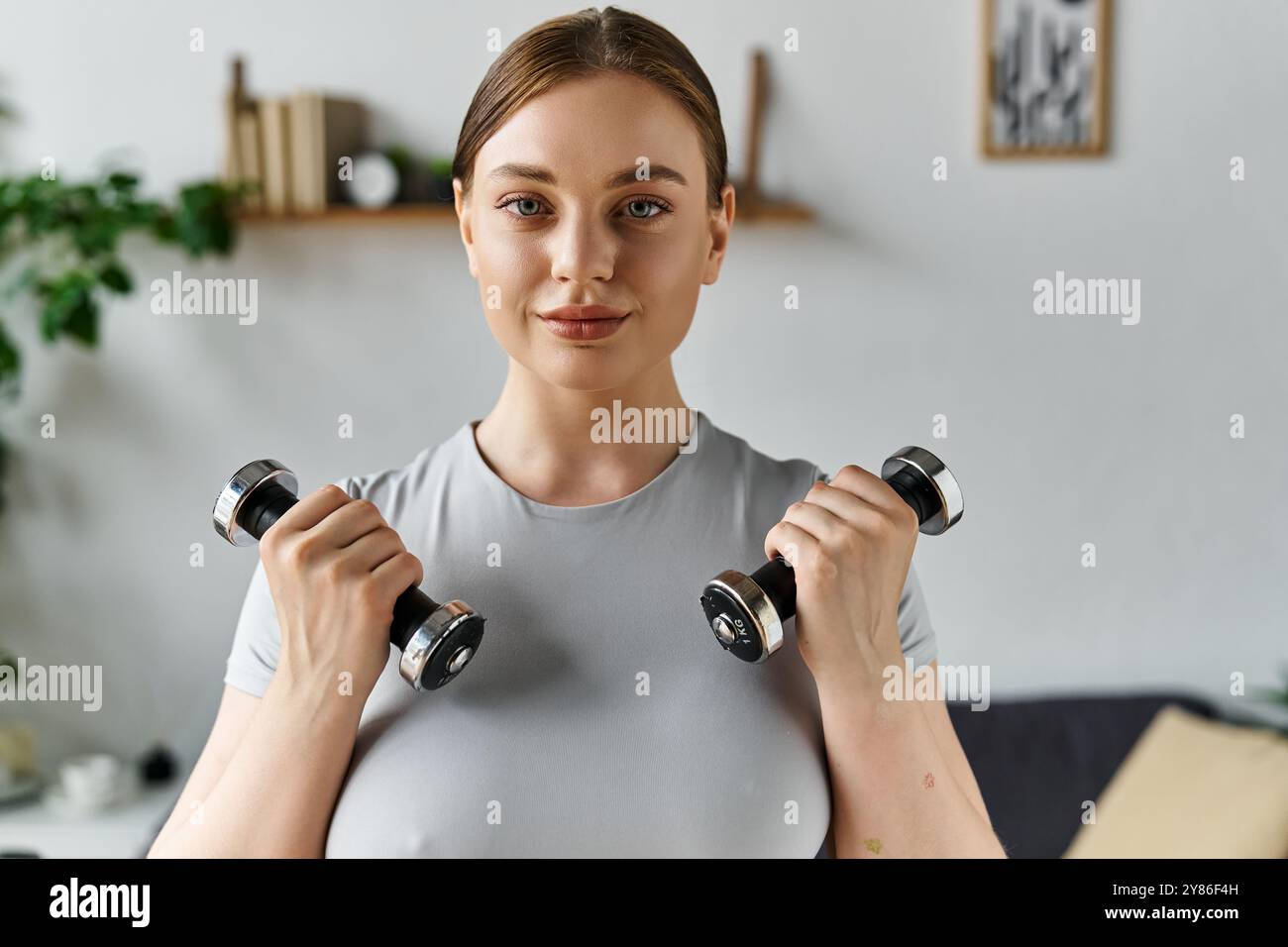 A dedicated young woman exercises at home, lifting weights while ...