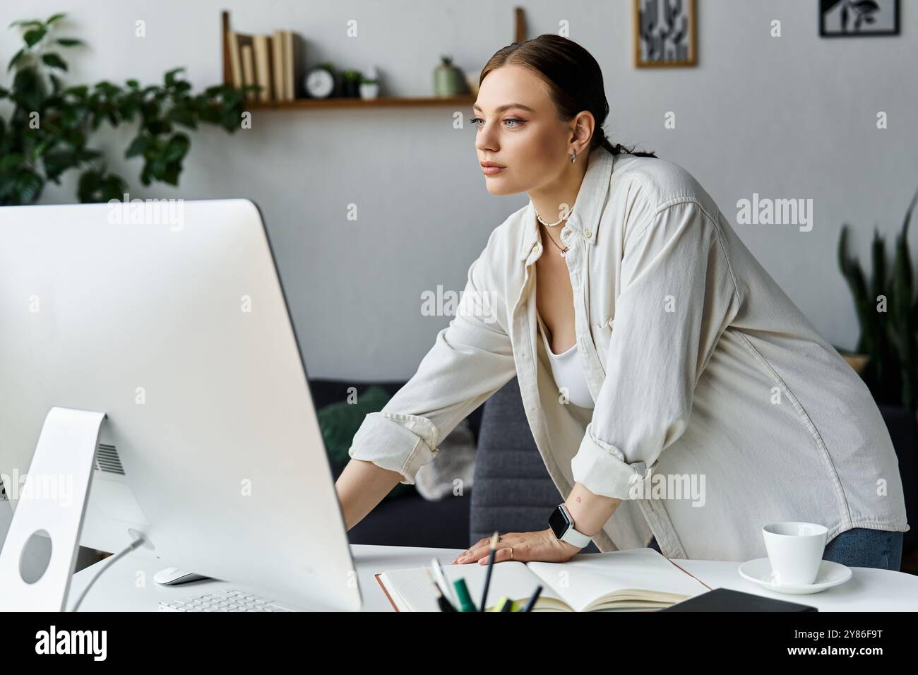 A dedicated young woman is working from home, leaning over her computer ...