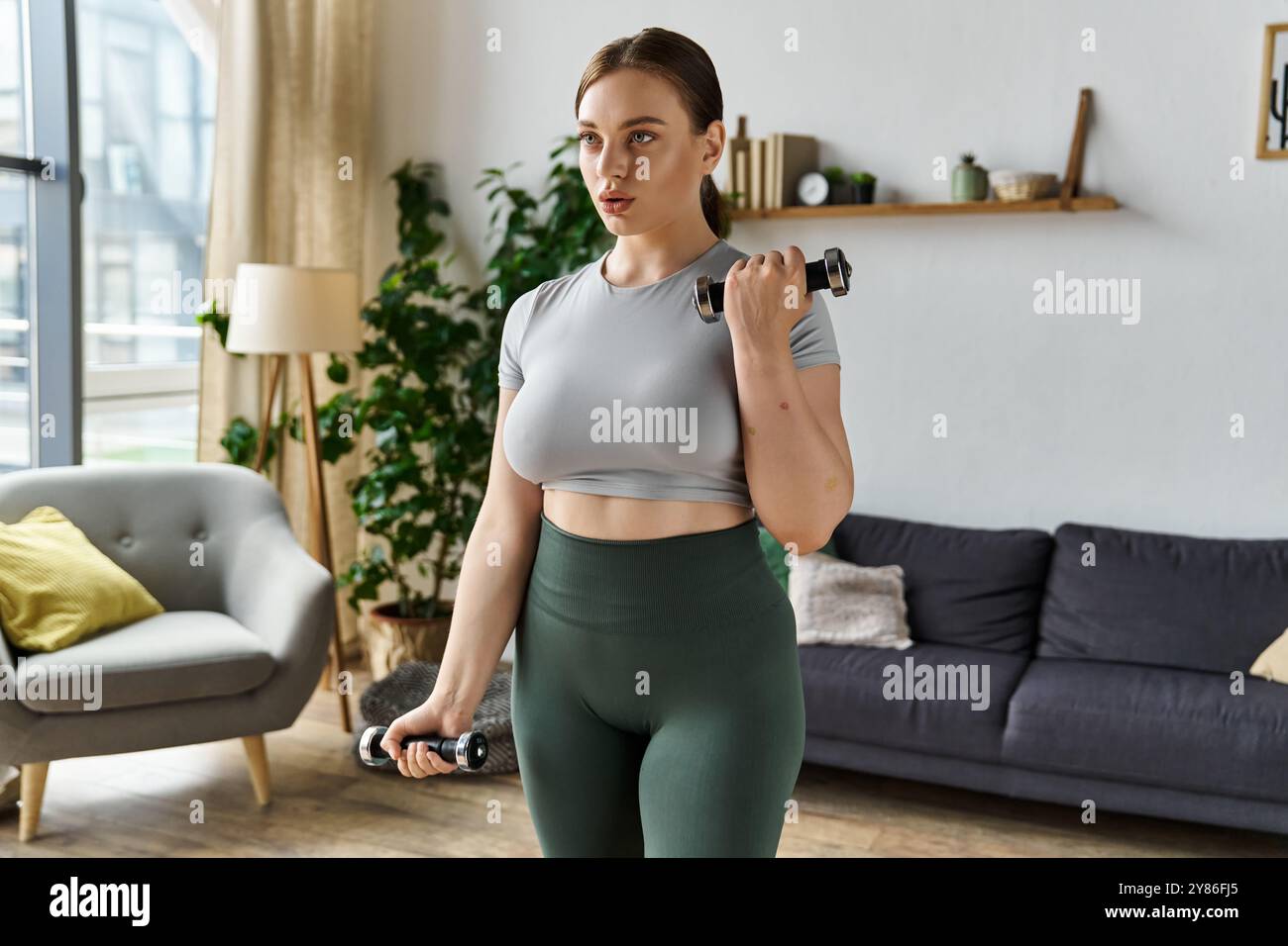 A young, sportive woman in active wear focuses on her strength training ...