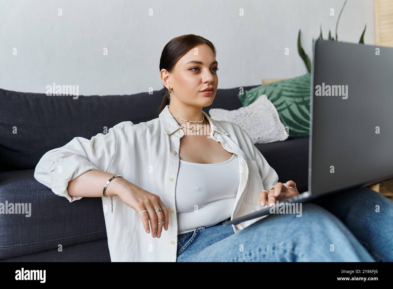 Concentrating on her work, a young woman sits casually near her laptop ...