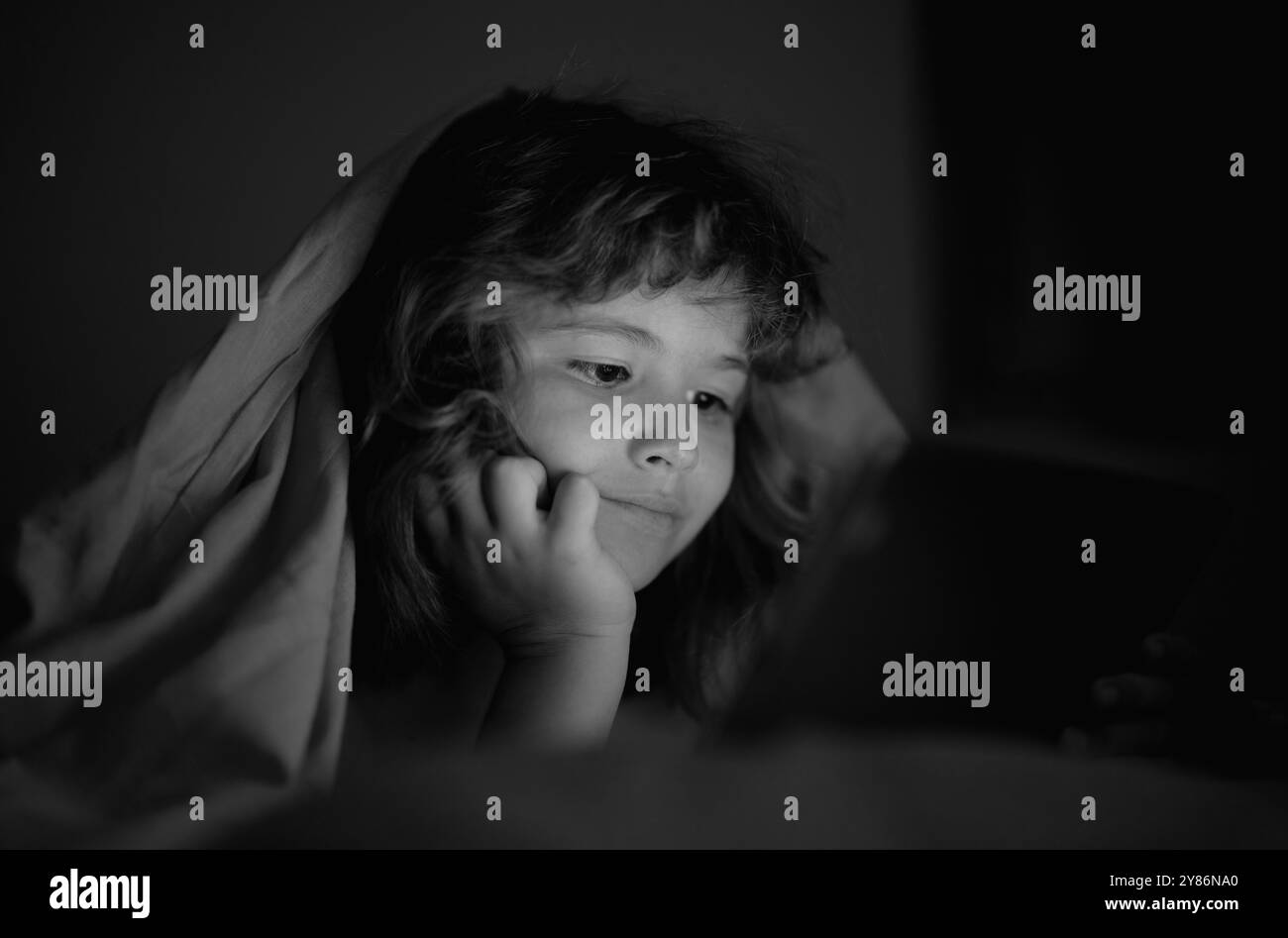 Kid alone at home. Cute little kid lying under blanket with tablet ...