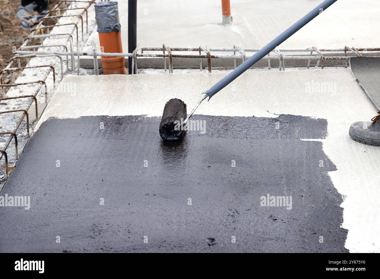 Worker applying a bituminous primer on a concrete slab at a ... Worker applying a bituminous primer on a concrete slab at a ...