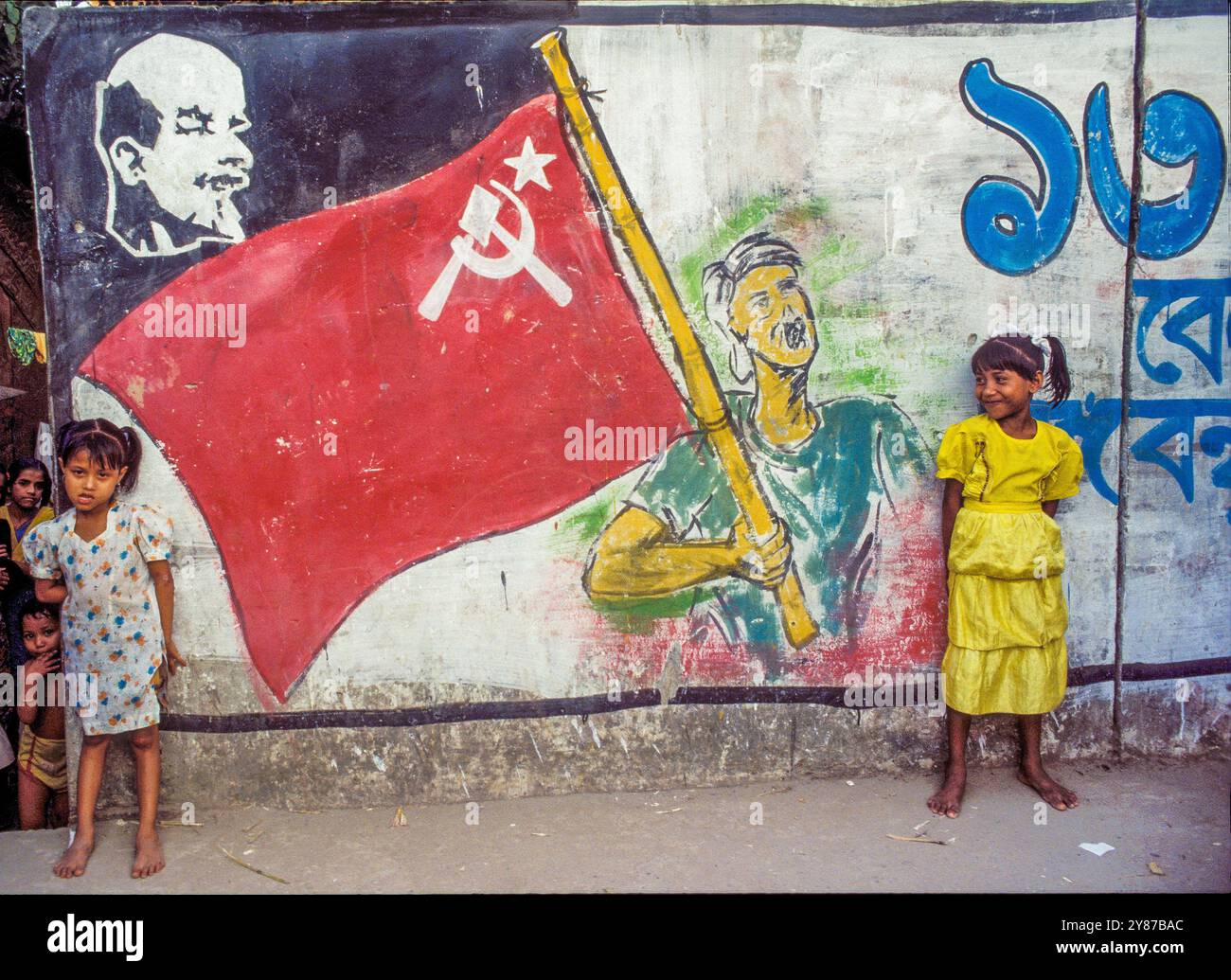 Bangladesh, Dhaka, two girls stand in front of a communist flag painted ...