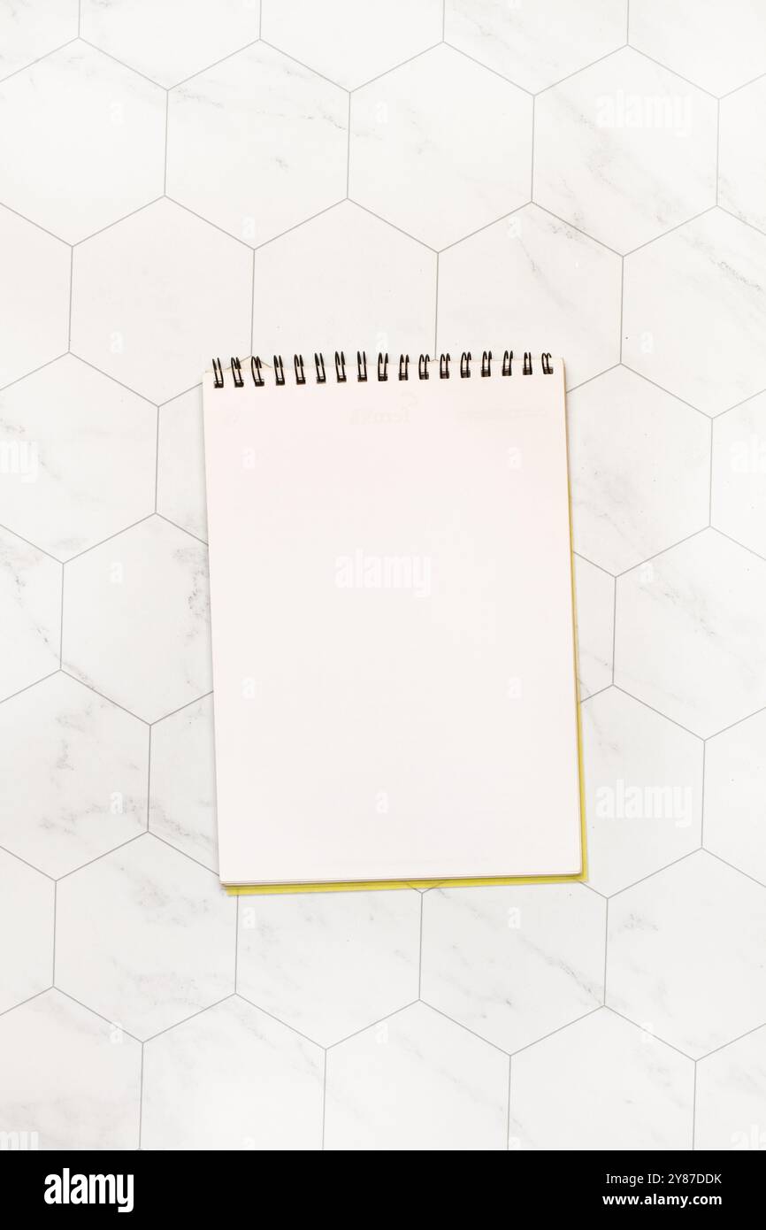 A spiral notepad open on a white page on a hexagonal tiled background ...