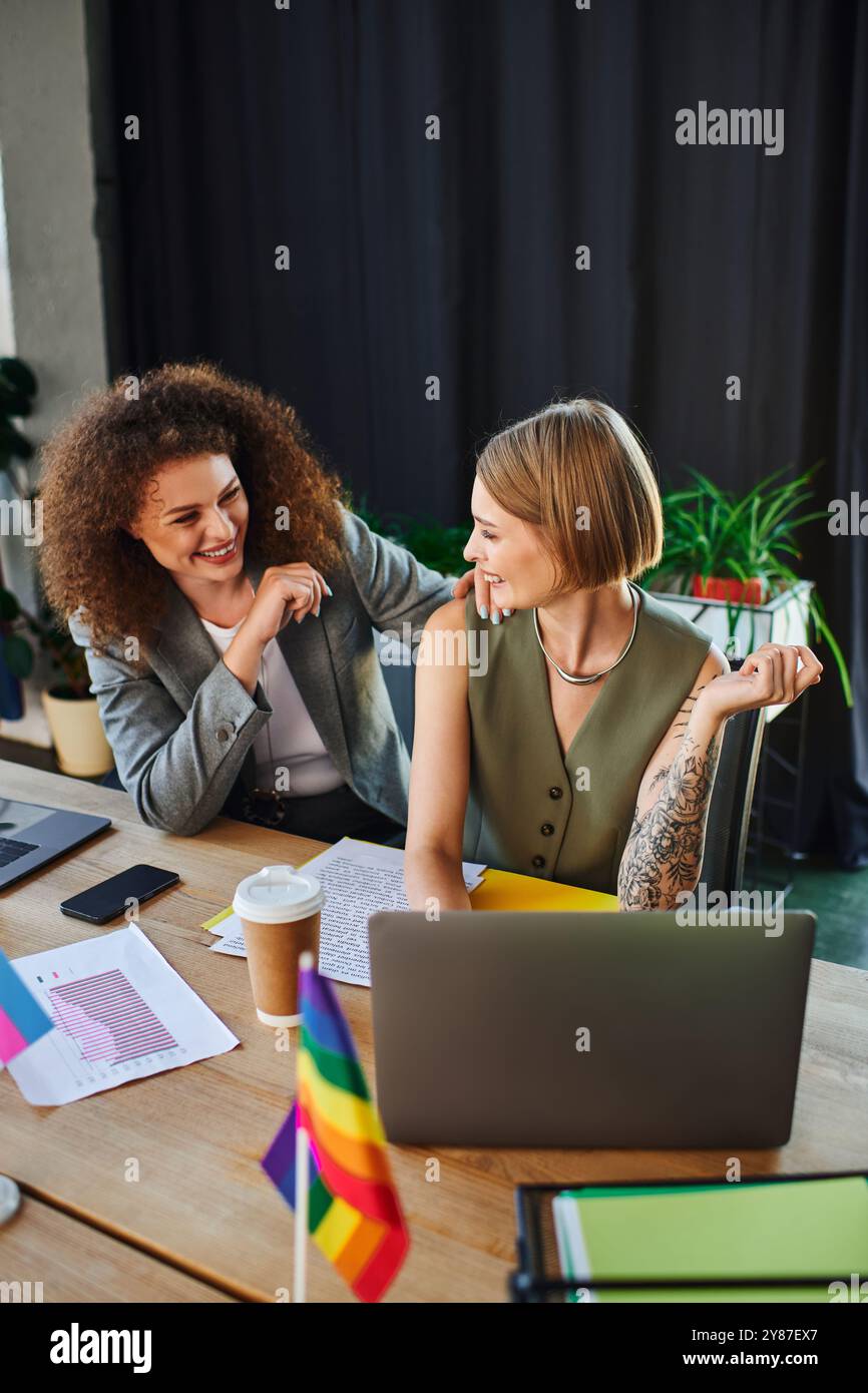 Two coworkers chat animatedly amid vibrant flags of the LGBTQ community ...