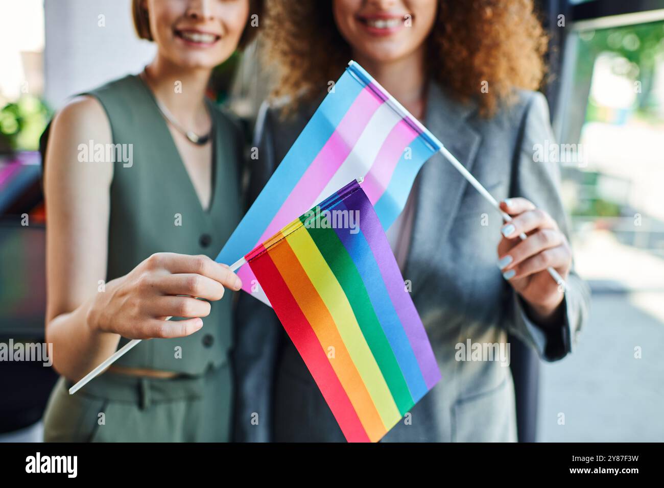 Two coworkers joyfully display pride flags, symbolizing inclusivity and ...
