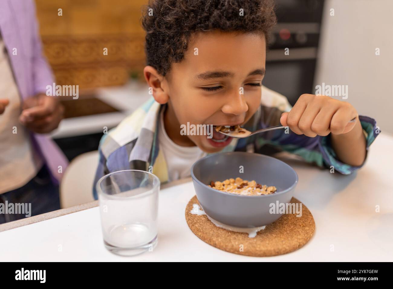Cute dark-skinned boy eating cereals and looking enjoyed Stock Photo ...