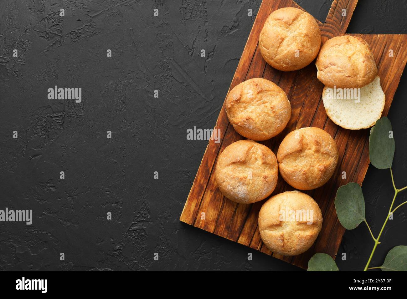 Homemade tasty buns and eucalyptus branch on black textured table, flat ...