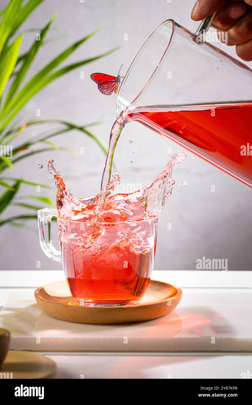 Pouring red fruit infusion and splashing from pitcher into glass on ...
