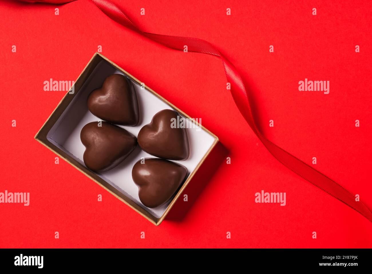 Heart shaped chocolate candies in a gift box on red background, top ...