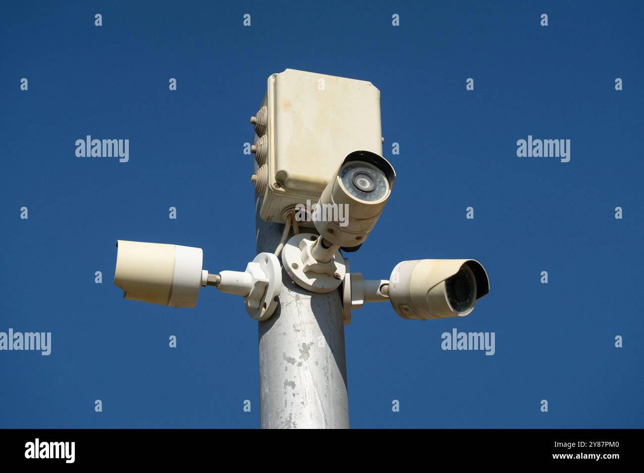 Three security cameras on a metal post , with a clear blue sky as ...