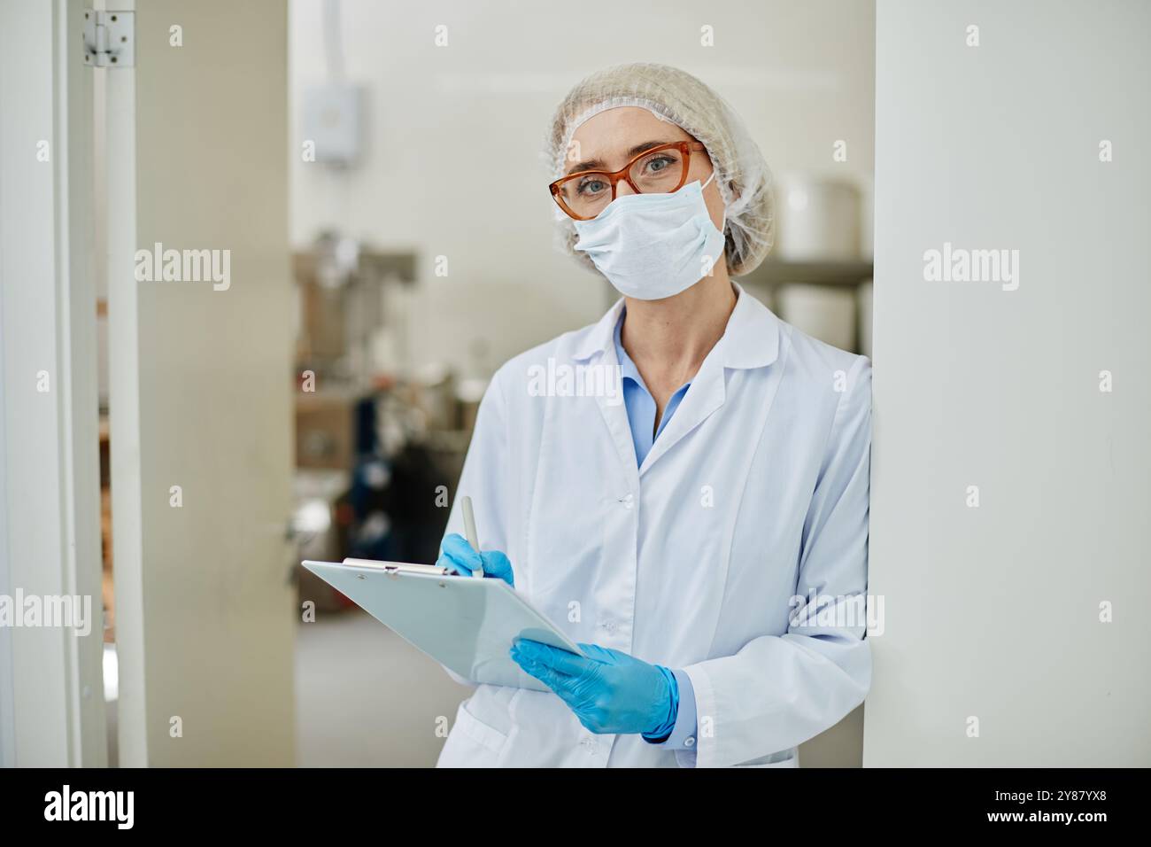 Waist up portrait of female process technician in lab coat taking notes ...