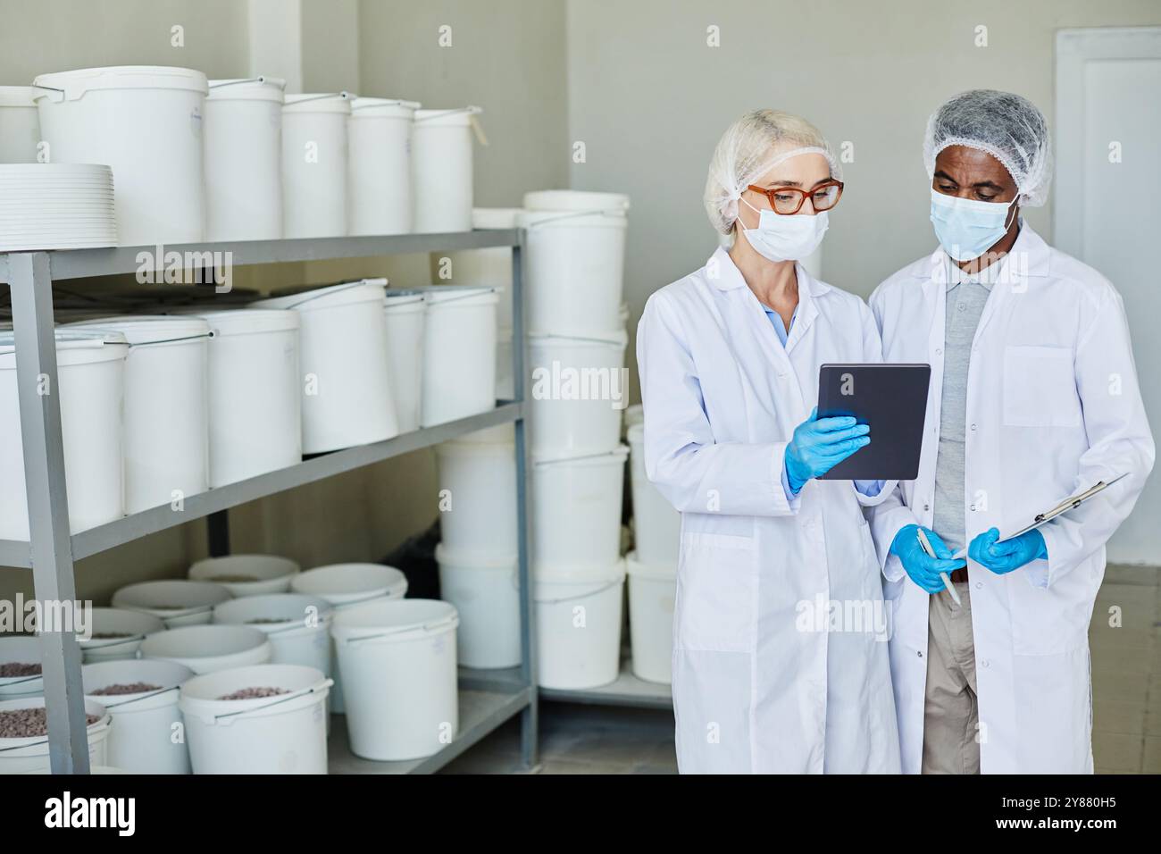 Medium shot of two supervisors in protective masks and lab coats using ...
