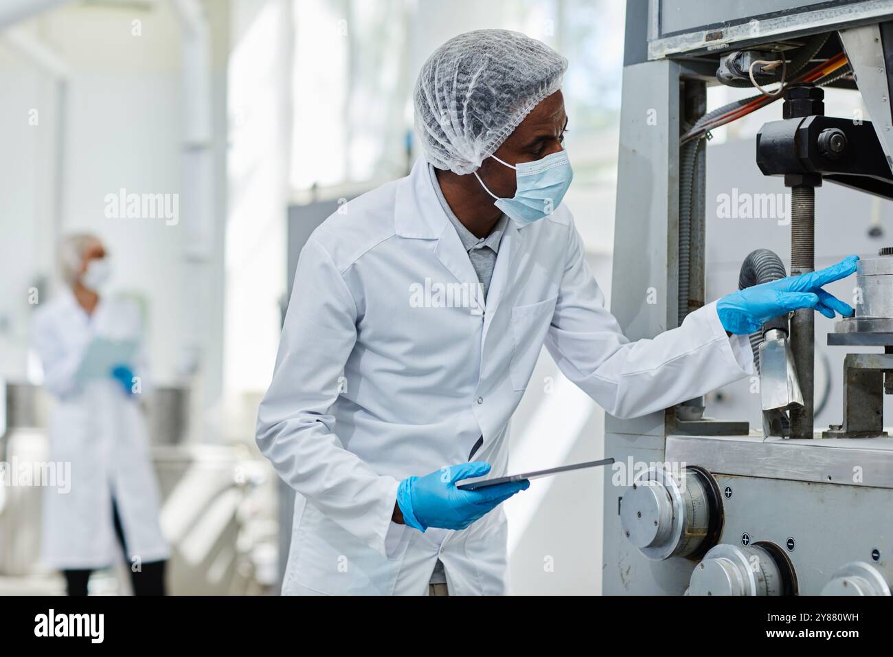 African American male process technician in lab coat looking inside ...