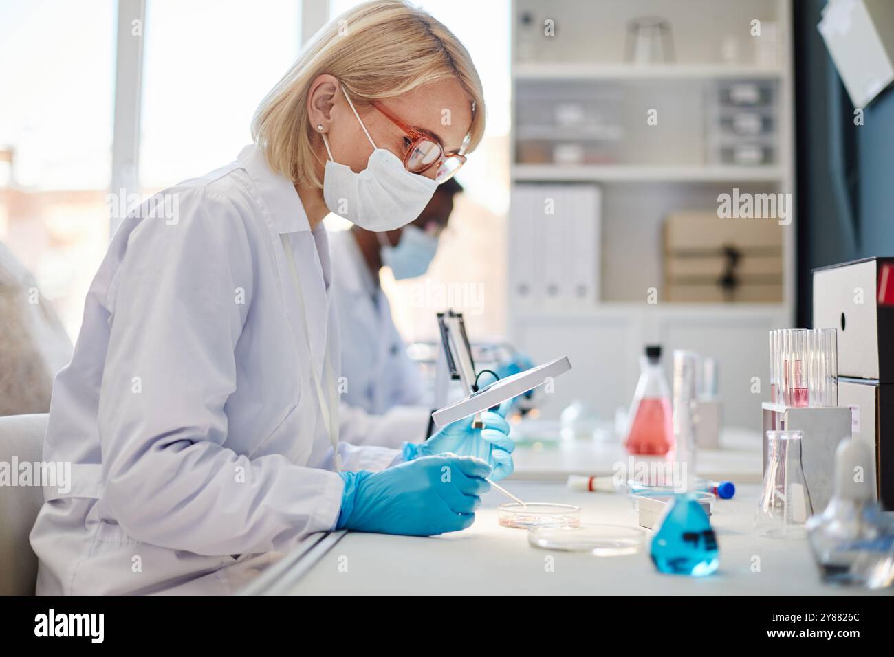 SIde view of female biochemist in protective mask looking through ...