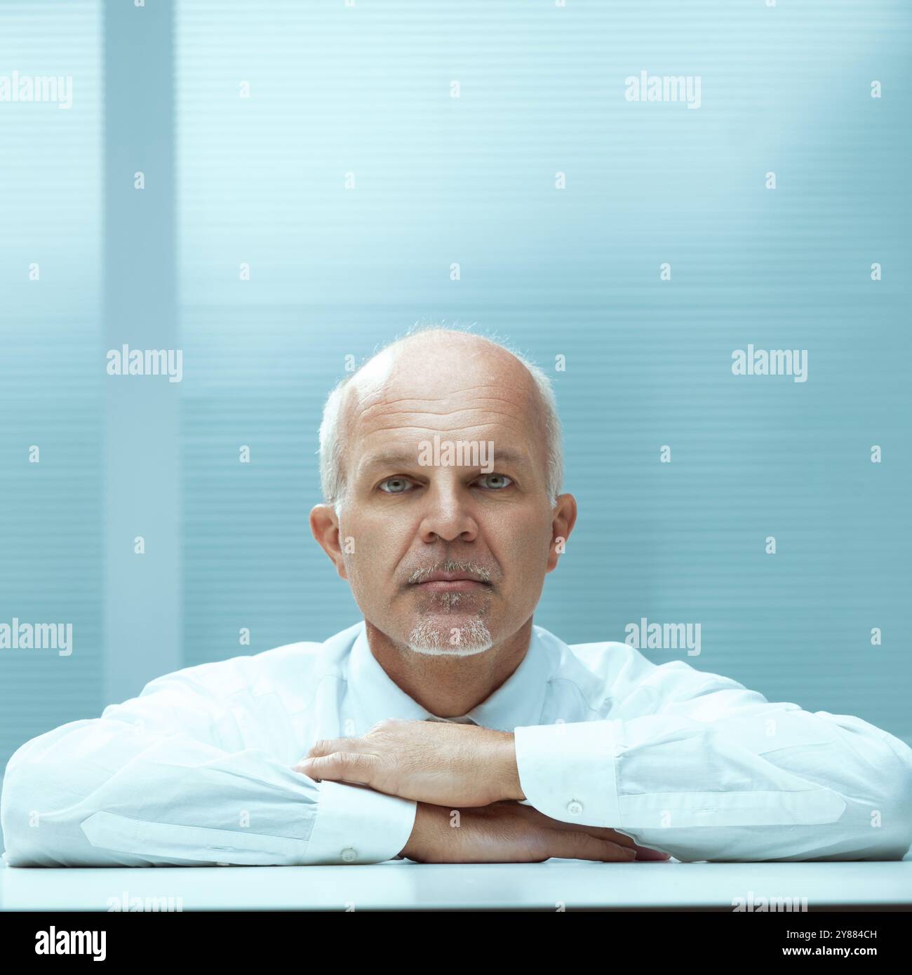 Confident mature businessman in office setting, arms crossed on desk ...