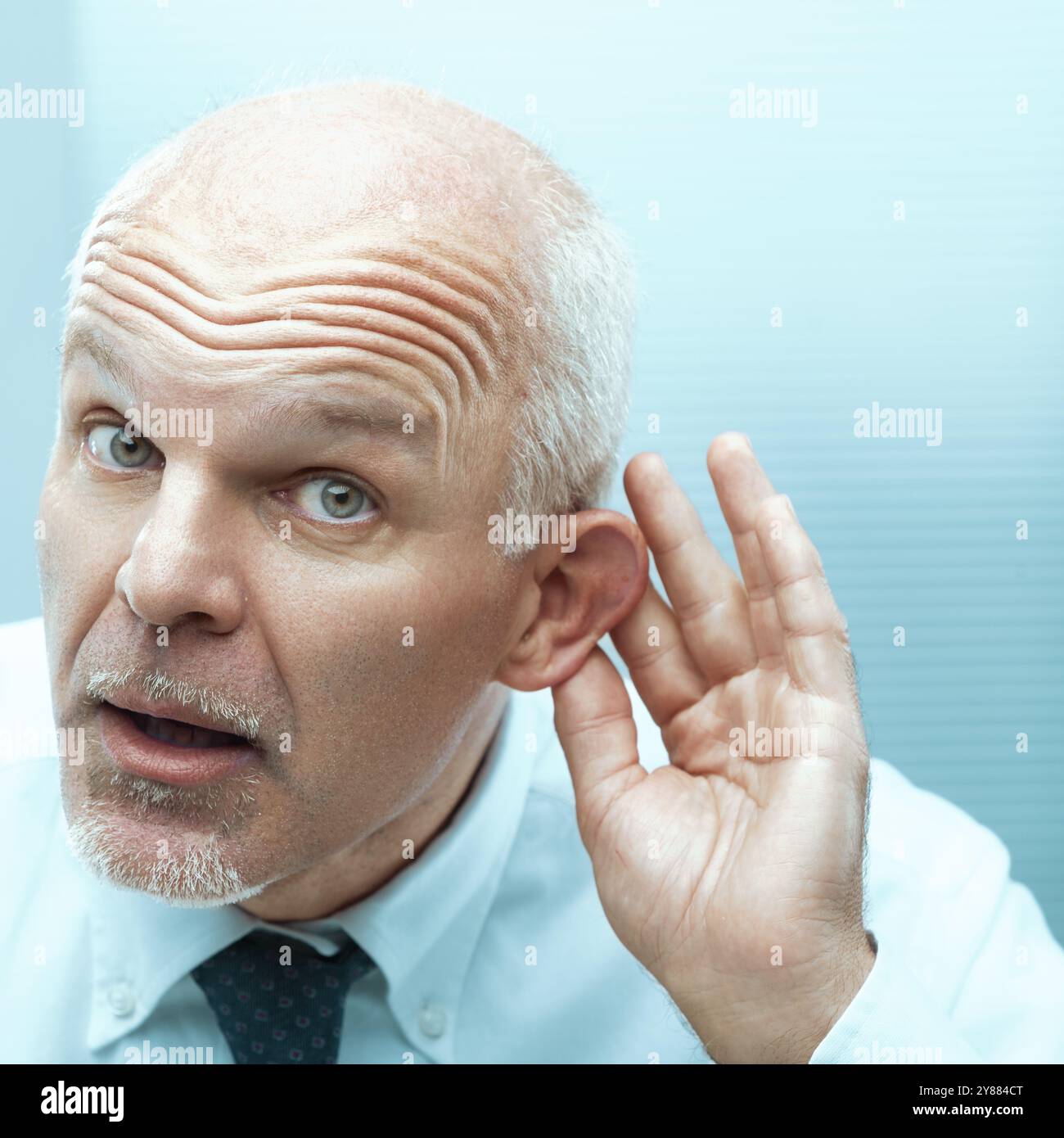 Curious businessman listens intently, cupping his ear with a concerned ...