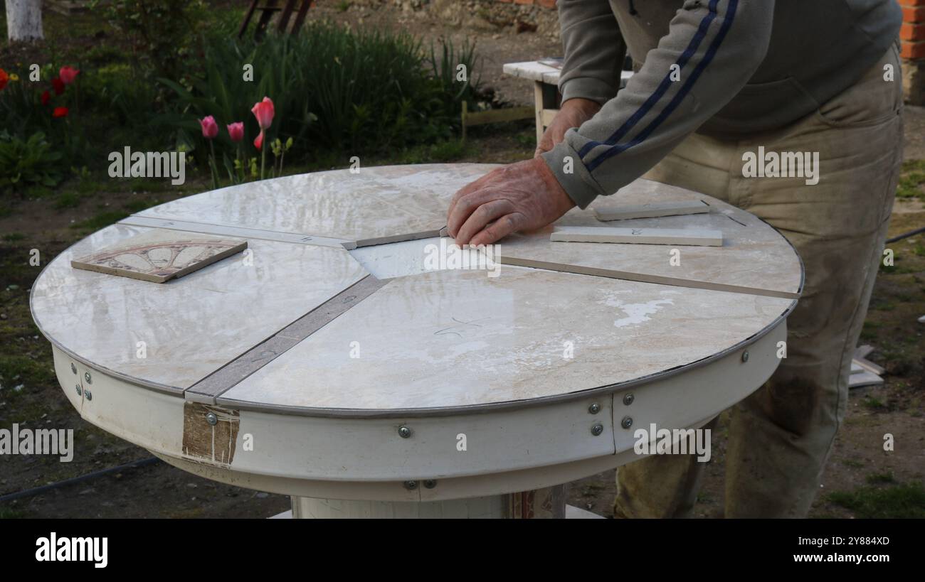craftsman lays out pieces of light brown ceramic tiles on round ...