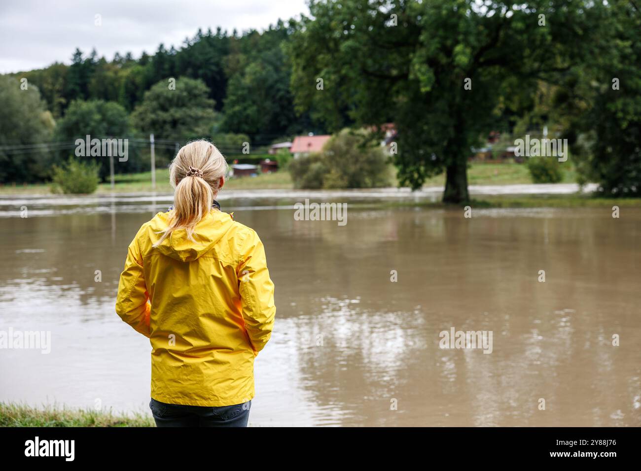 Flooded river. Worried woman looking at overflowing water during flood. Extreme weather and ...