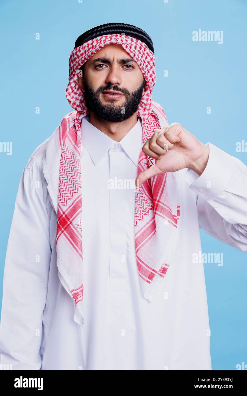 Arab man in traditional robe and headdress showing thumb down studio ...