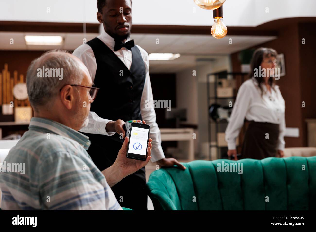 Retired senior male traveler in cozy lounge area paying with smartphone ...