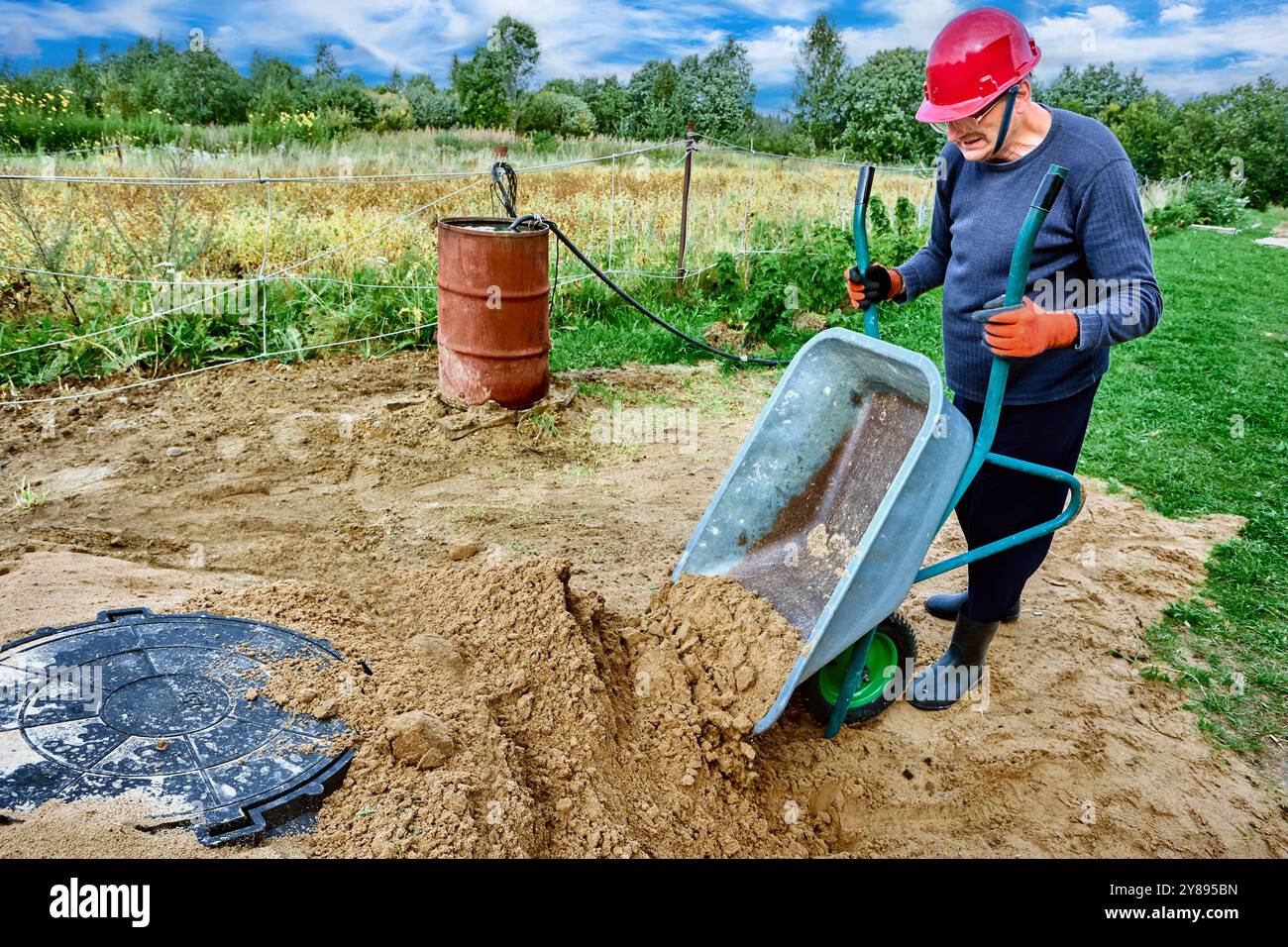 Construction worker pours sand from wheelbarrow around manhole cover ...