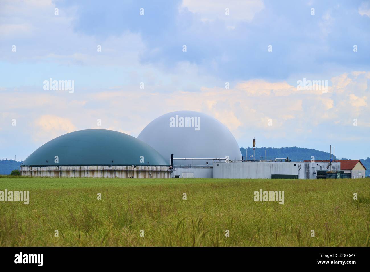 Modern biogas plant in the middle of green fields under a cloudy blue ...