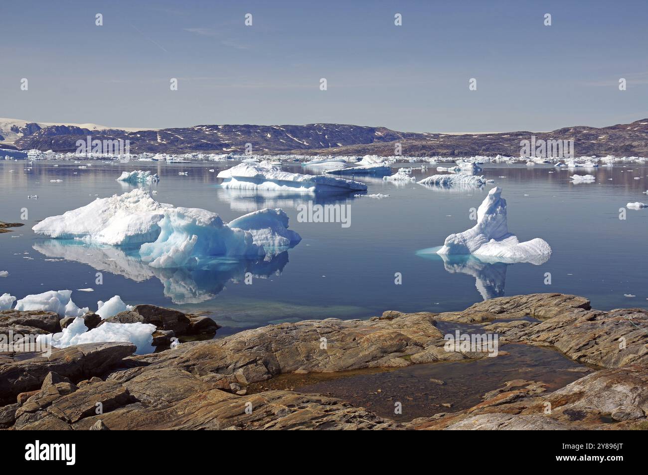 A calm fjord with floating icebergs and rocks under a clear sky ...