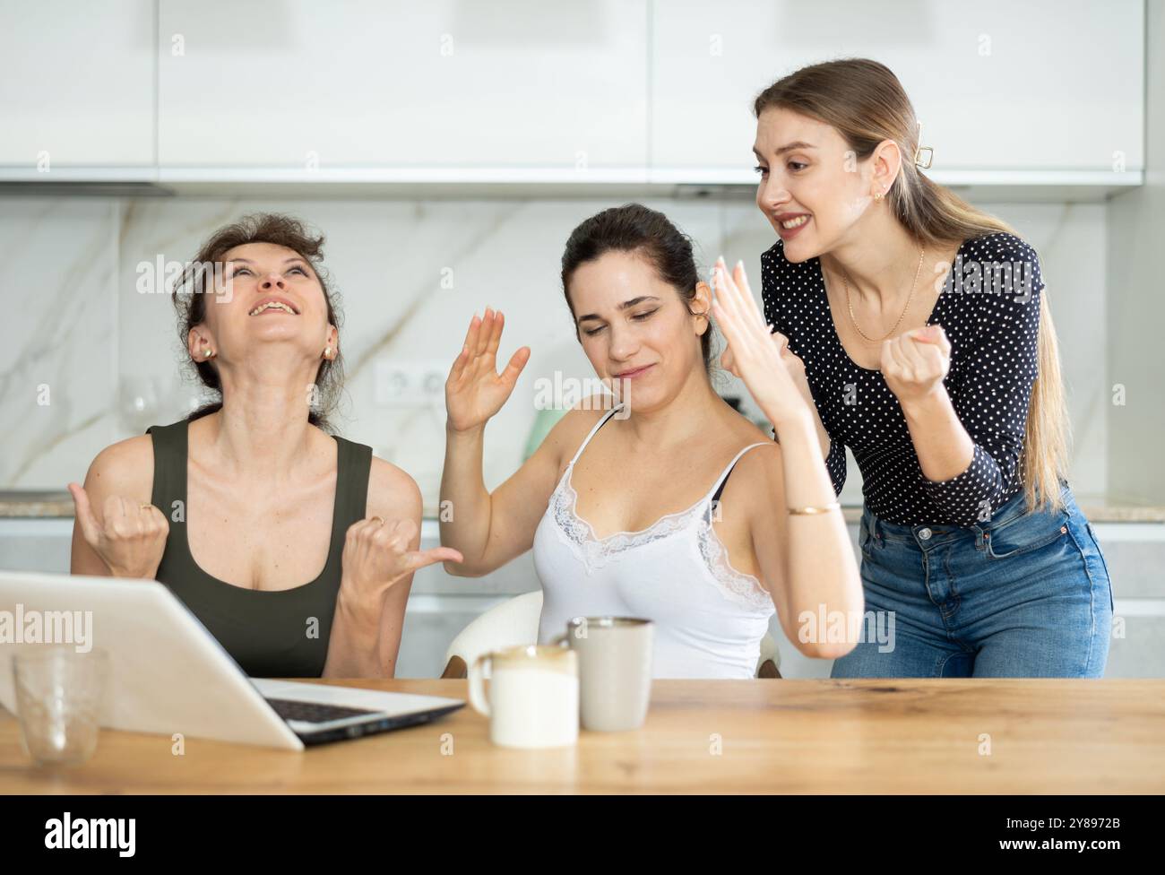 Three happy middle-aged woman expressing joy for winning in the kitchen ...