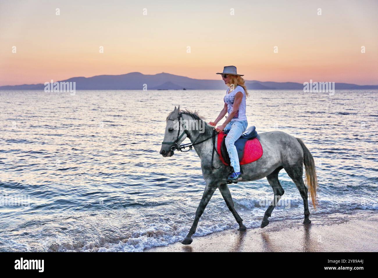 Young woman riding a horse at sunset on the beach of Plaka in Naxos ...