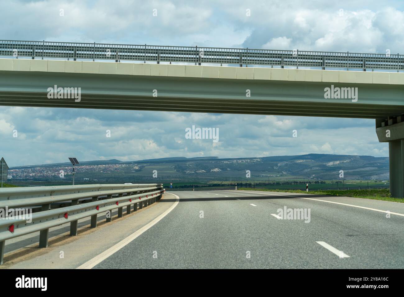 A bridge spans a road with a clear sky above. The bridge is a large ...