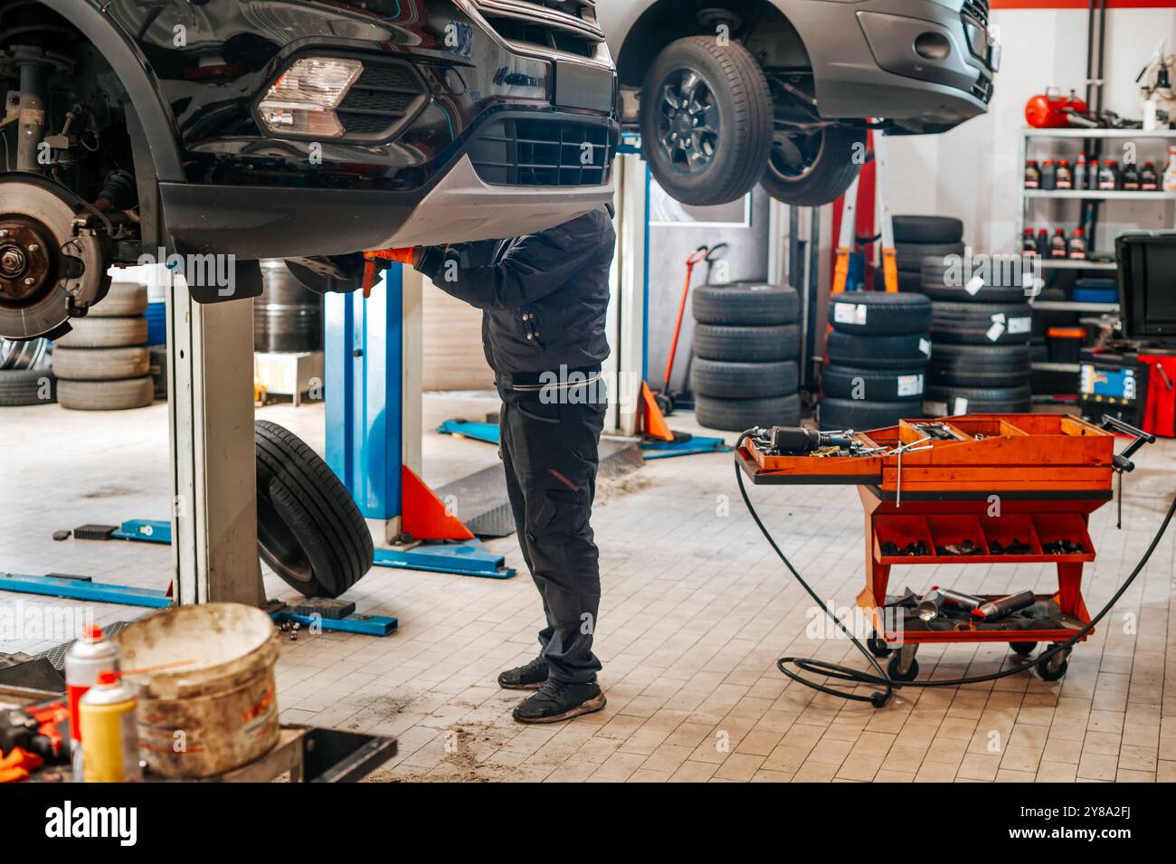 Mechanic is working under a car lifted on a hydraulic lift, fixing the ...