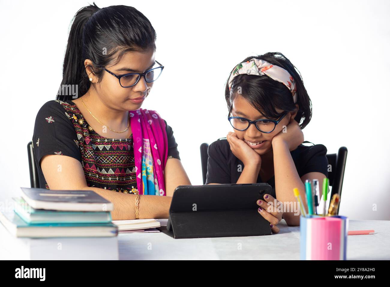 An Indian girl student studying with tablet besides her mother on white ...
