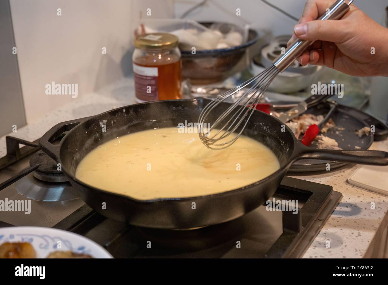 Hand holding a whisk and stirring sauce in a cast iron pan. Home ...