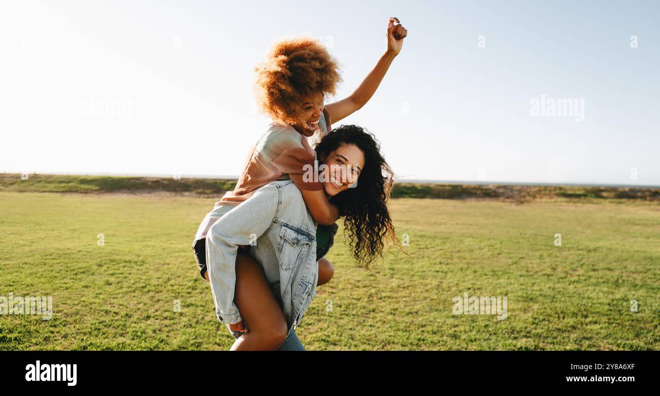 Two playful friends sharing a piggyback ride in a sunny park ...