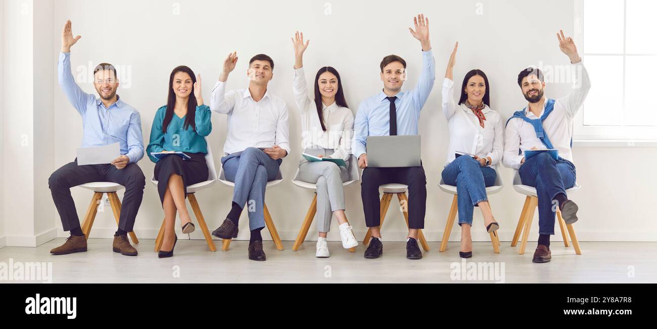 Company employees raising hands to vote at conference sitting on chairs ...