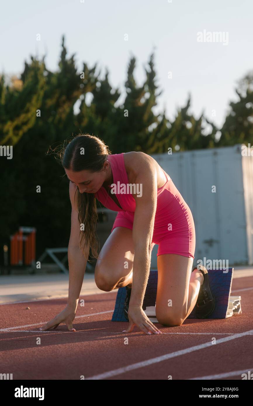 Female track athlete getting into blocks to sprint out Stock Photo - Alamy