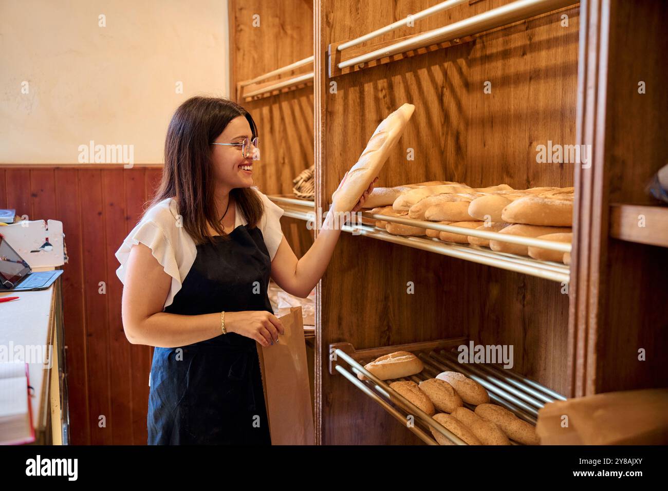 A smiling baker selecting fresh bread in a cozy bakery during the day ...