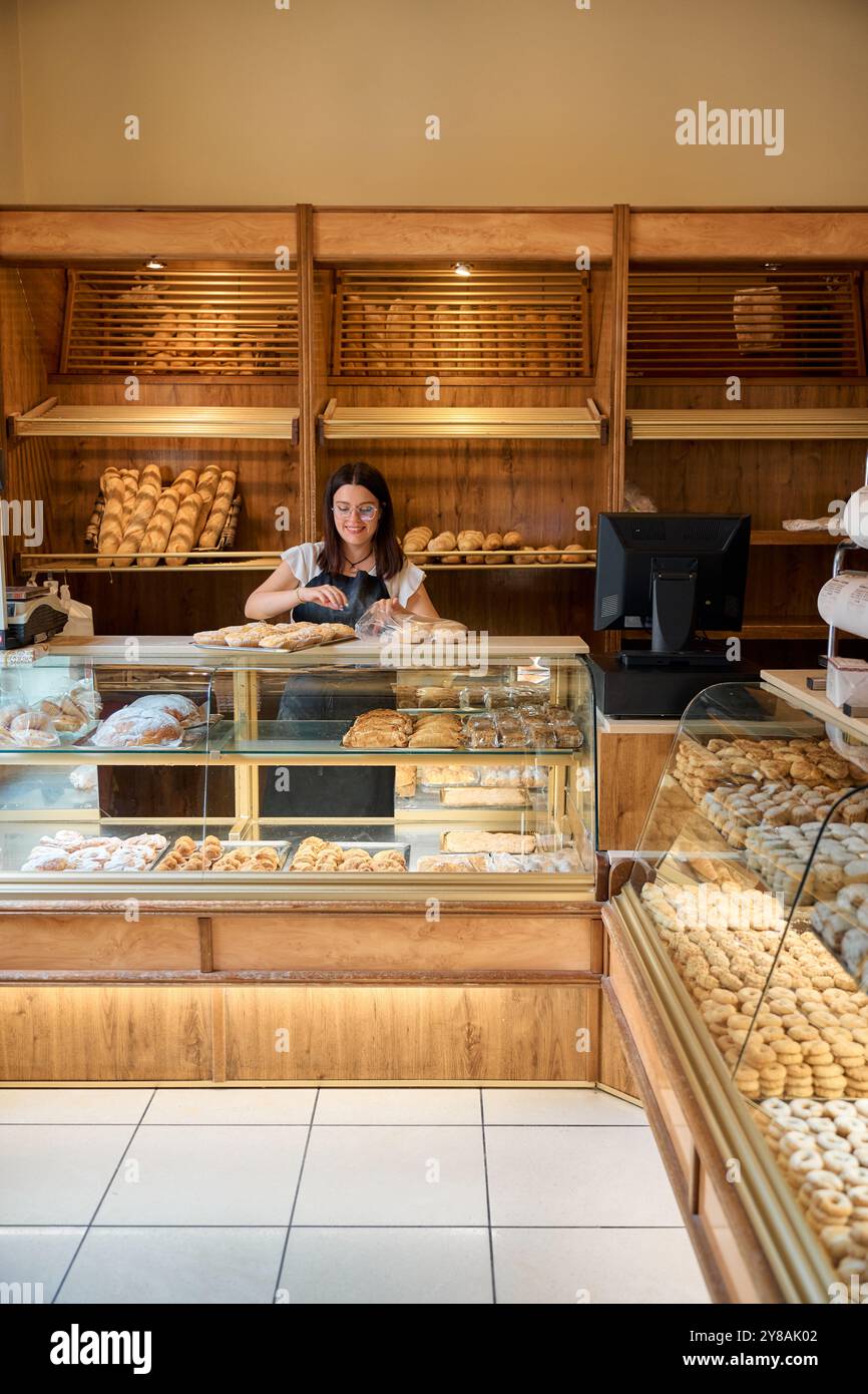 Baker arranging fresh pastries in a cozy bakery during morning hours ...