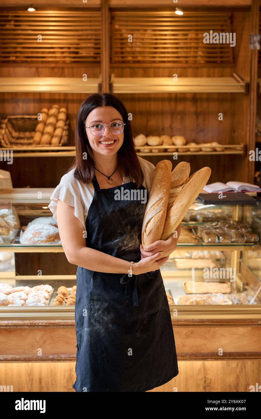 Young baker holding fresh bread loaves in a cozy bakery setting Stock ...