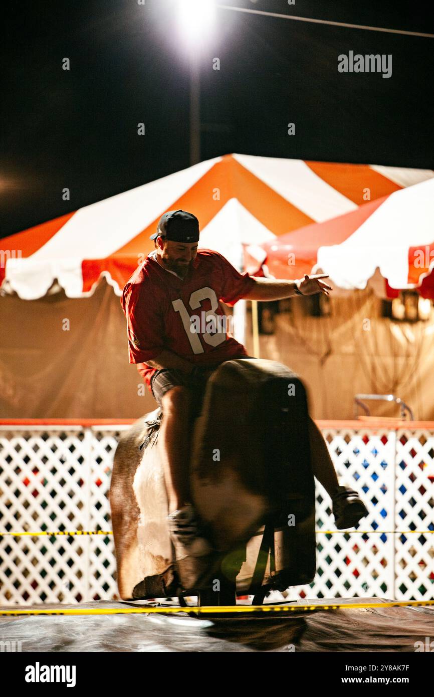 Man riding mechanical bull at carnival at night Stock Photo - Alamy