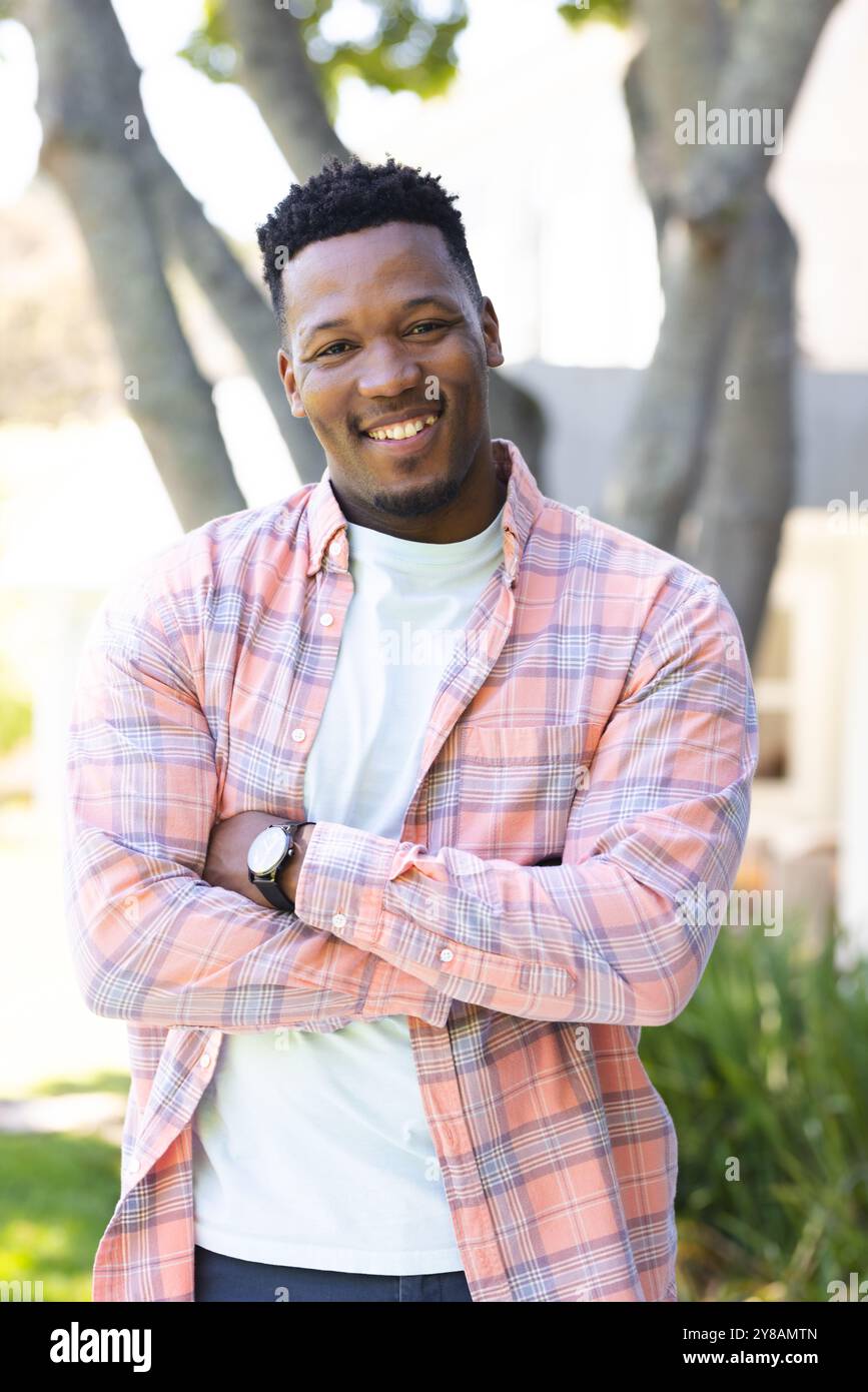 Happy african american man walking with arms crossed in sunny garden ...