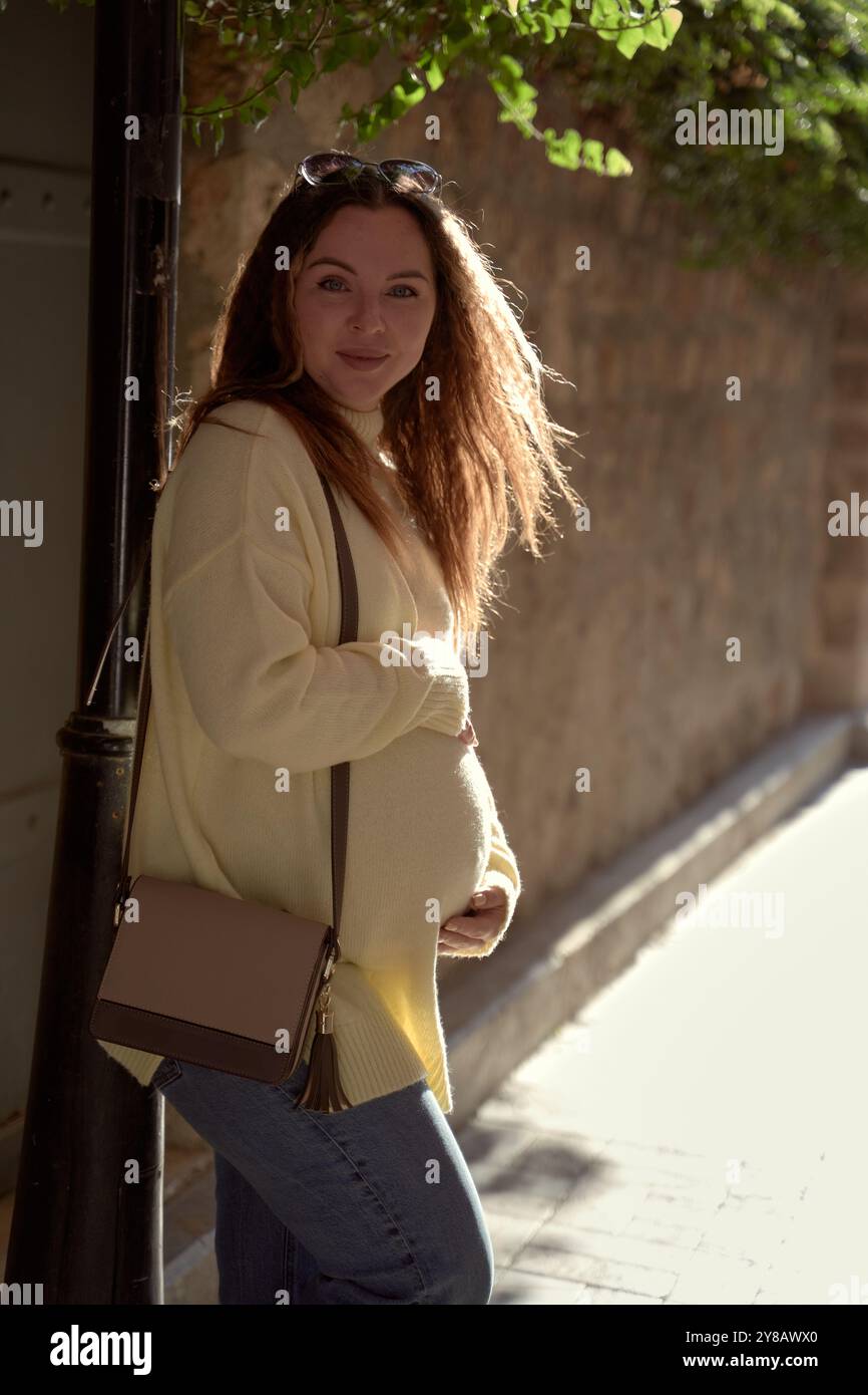 Expecting mother poses joyfully outdoors in a sunny setting during her ...
