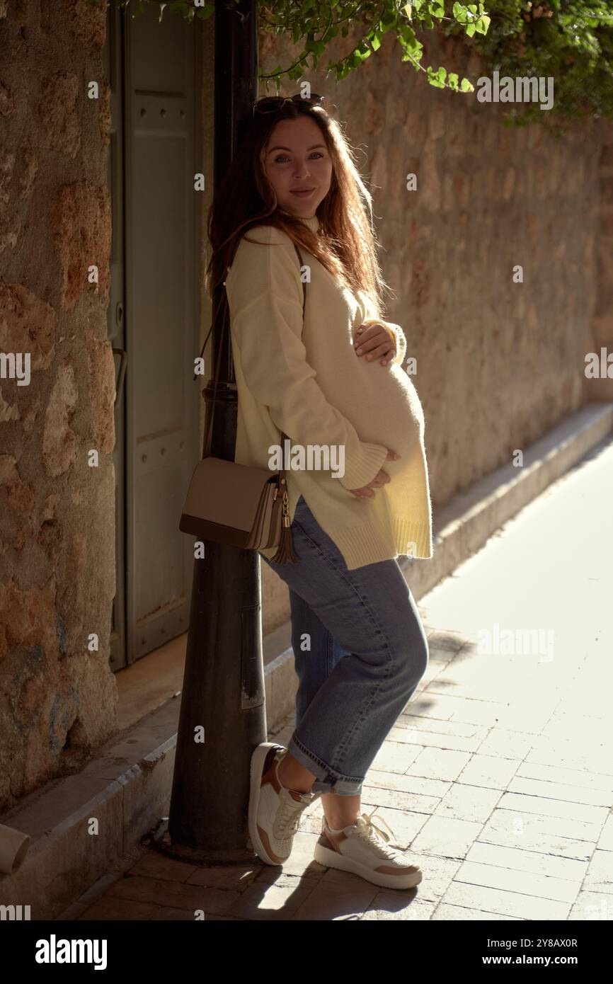 Expecting mother poses joyfully outdoors in a sunny setting during her ...