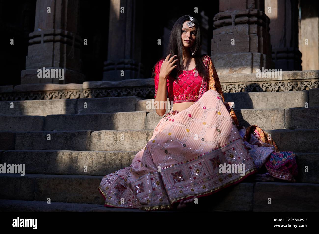 A young woman in traditional pink Indian clothing and skirt sits on the ...
