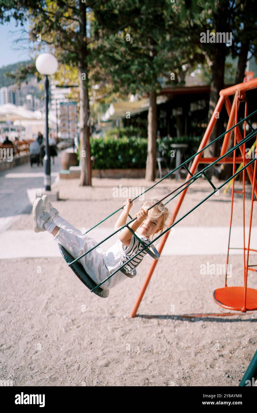 Little girl swings on a colorful swing on a playground in a park, looking to the side Stock ...